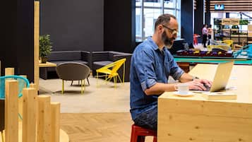 Um homem trabalha num laptop num espaço de escritório moderno com móveis de madeira e mesa de bilhar.