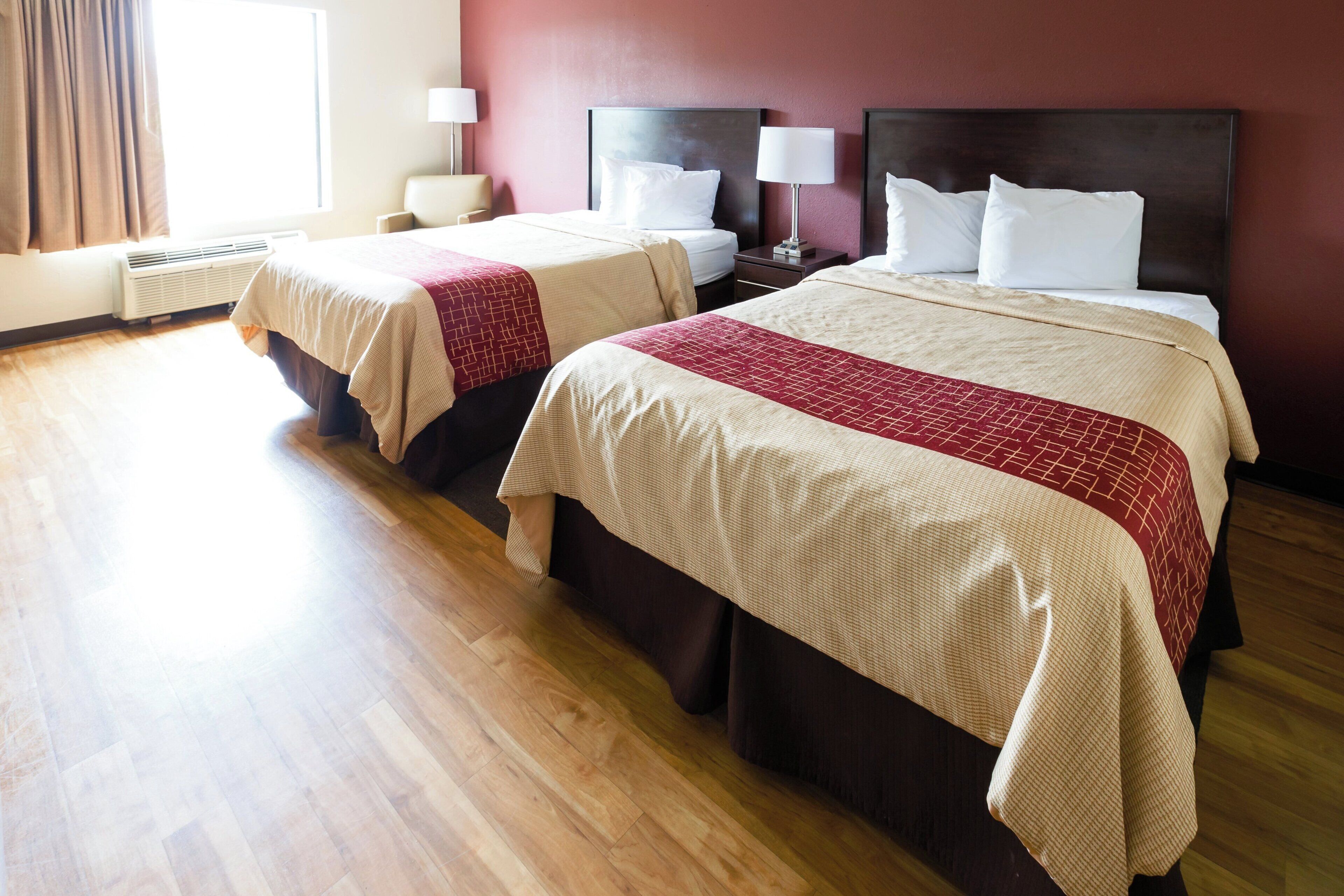Quarto de hotel com duas camas, uma mesa de cabeceira, uma luminária e uma janela com cortinas.
