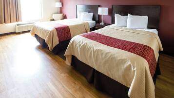 Quarto de hotel com duas camas, uma mesa de cabeceira, uma luminária e uma janela com cortinas.