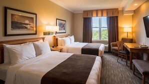Quarto de hotel com duas camas, uma escrivaninha, uma cadeira, uma televisão e uma janela com cortinas.