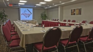 Uma sala de conferências com uma mesa comprida, cadeiras vermelhas e uma tela de projetor exibindo 'FUTURE INNS HALIFAX'.