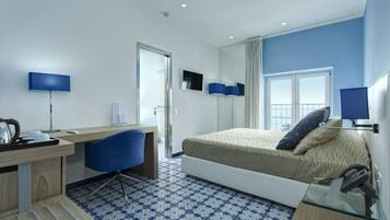 Quarto de hotel moderno com cama, escrivaninha e cadeira, uma janela grande e vista para a cidade.