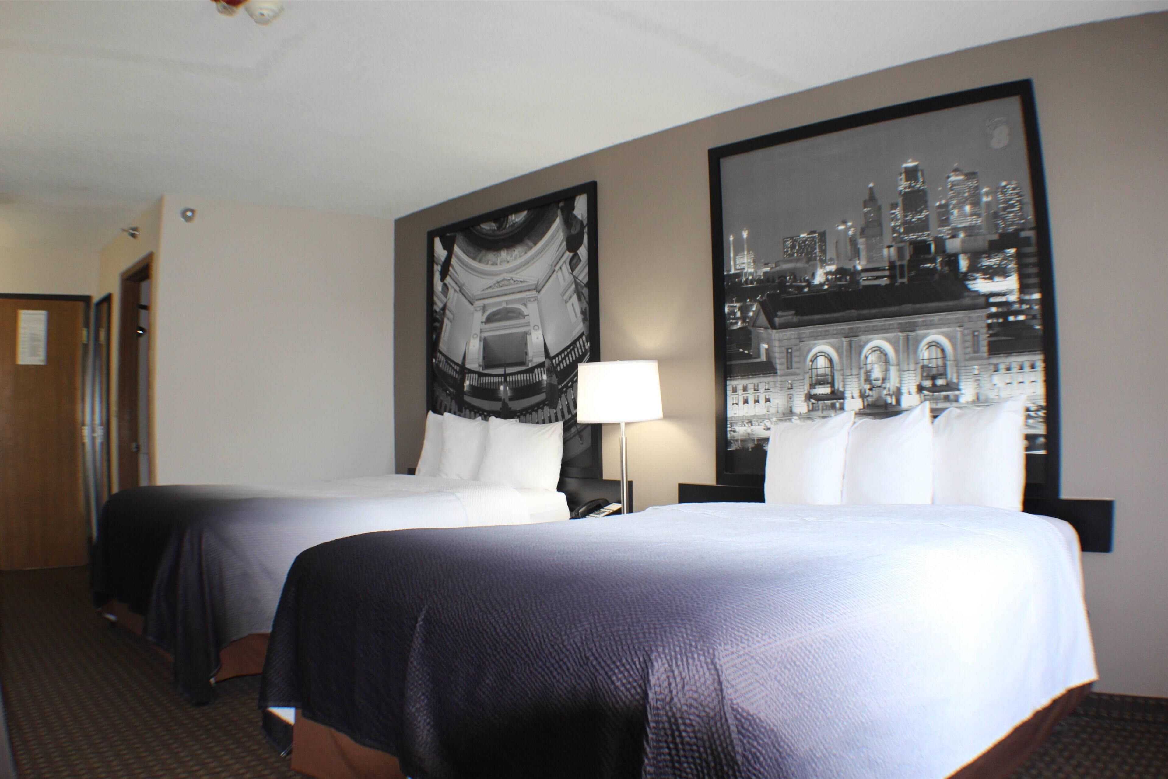 Quarto de hotel com duas camas, uma mesa de cabeceira, um abajur e duas grandes molduras na parede.