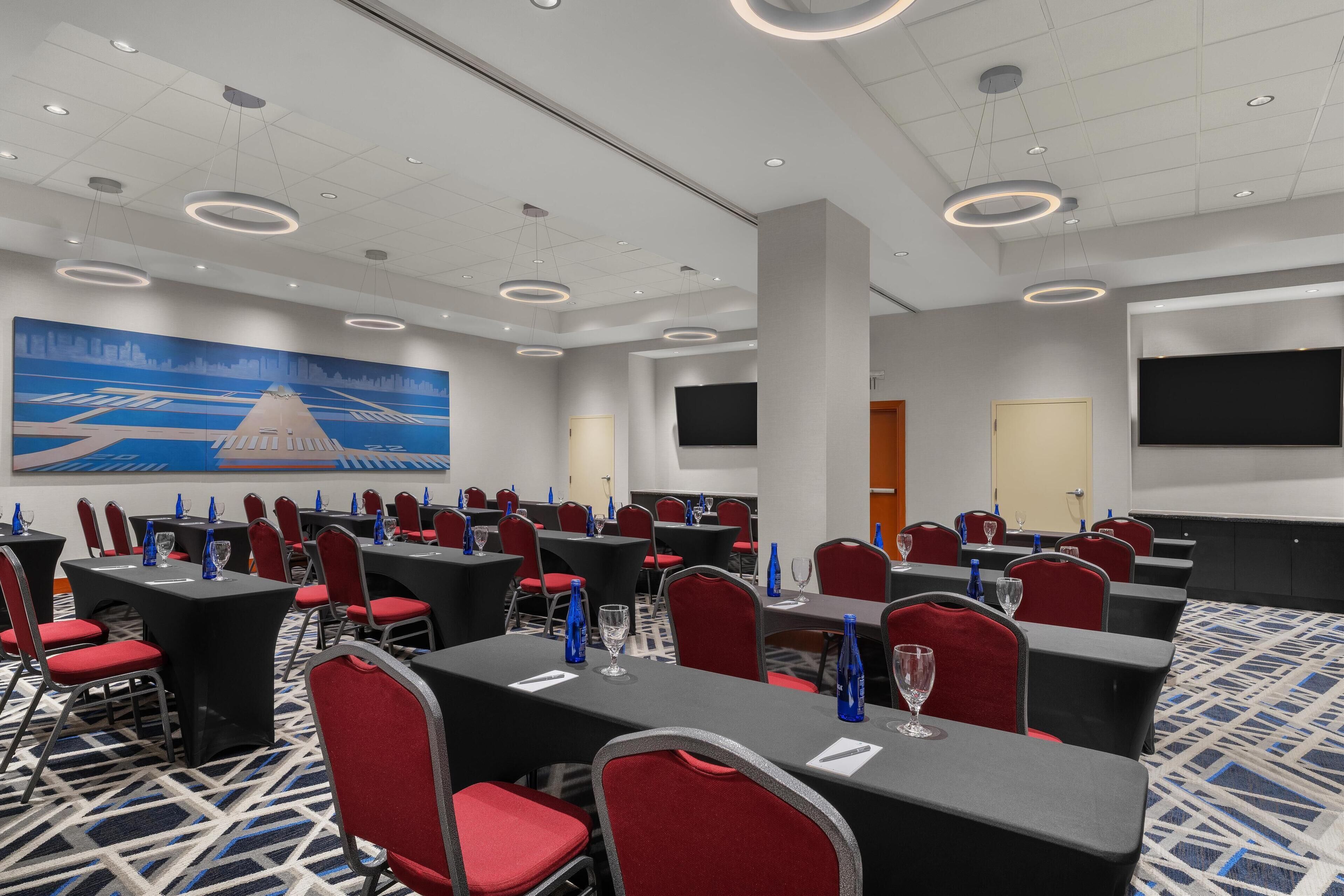 Uma sala de conferências com mesas, cadeiras e uma tela grande.