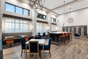 Uma sala de jantar moderna com pé direito alto, grandes janelas e móveis contemporâneos.