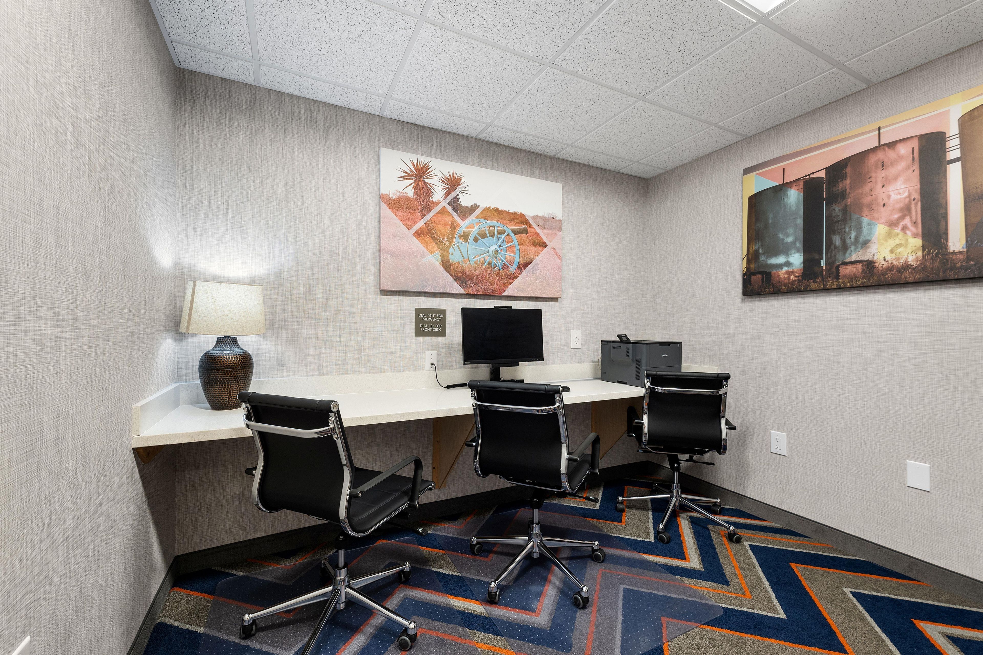 Sala de conferência com uma mesa branca, quatro cadeiras de escritório pretas, um computador e uma luminária.
