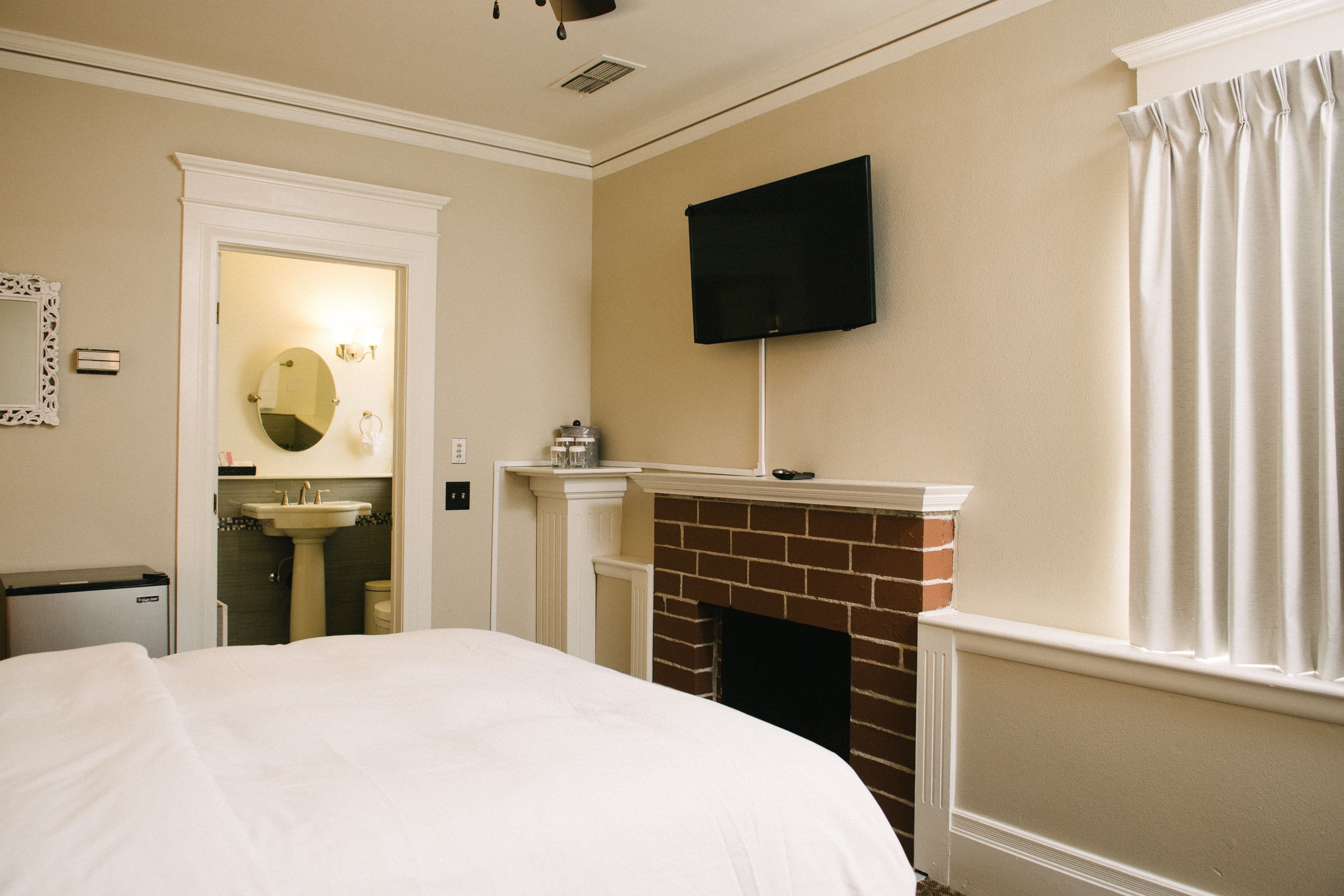 Quarto de hotel com uma cama grande, lareira, televisão na parede e banheiro com pia e espelho.