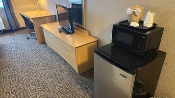 Quarto de hotel compacto com escrivaninha, mini-geladeira, micro-ondas e lixeira.