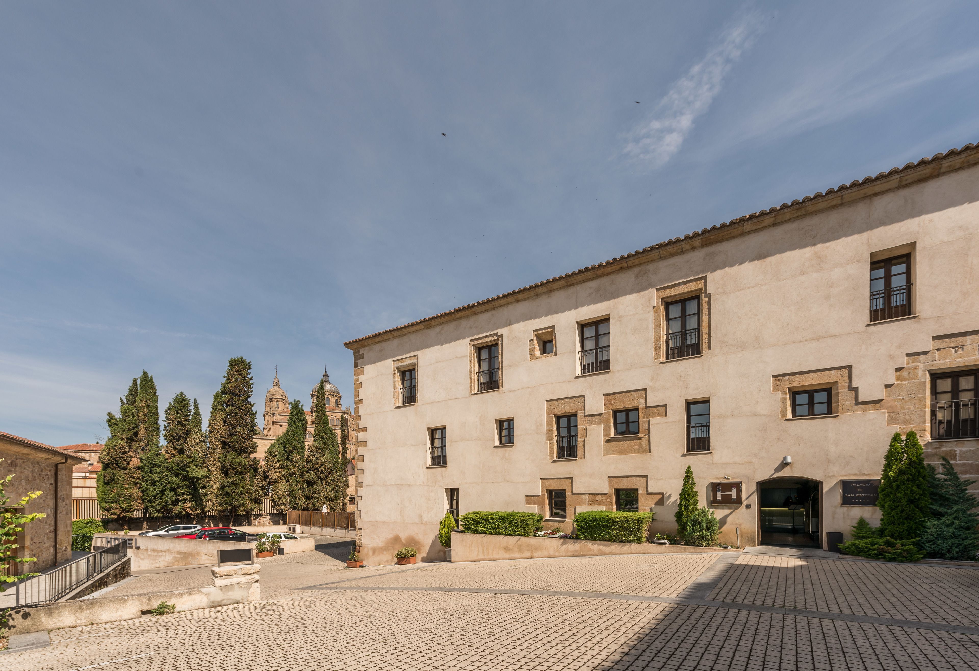 Um edifício histórico com fachada simétrica, várias janelas e um pátio pavimentado.