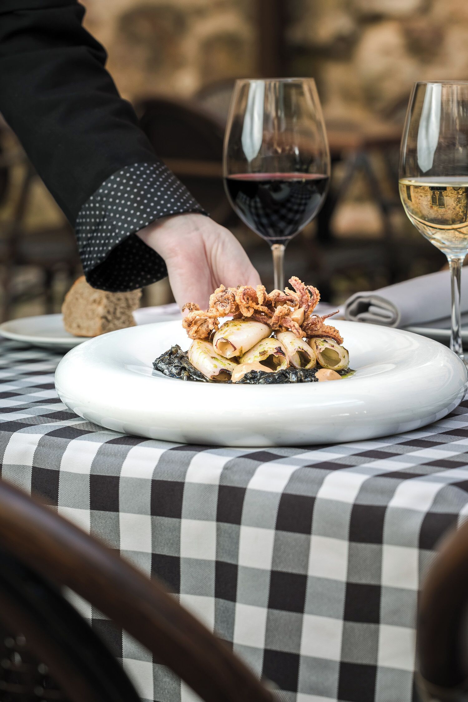 Um prato de massa com frutos do mar e um copo de vinho tinto sobre uma mesa com toalha xadrez.