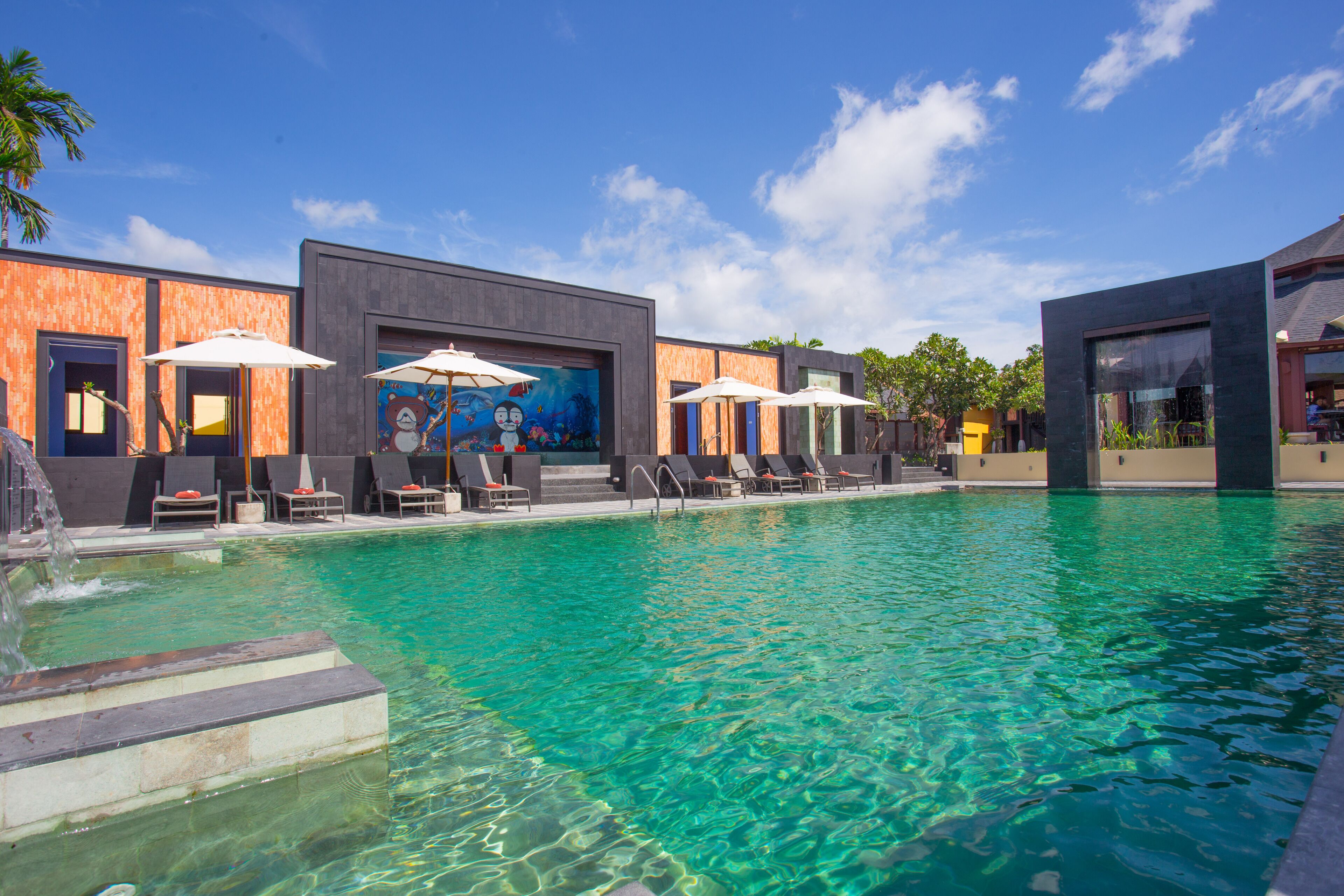Piscina com espreguiçadeiras e guarda-sóis, rodeada por edifícios modernos com grandes janelas.