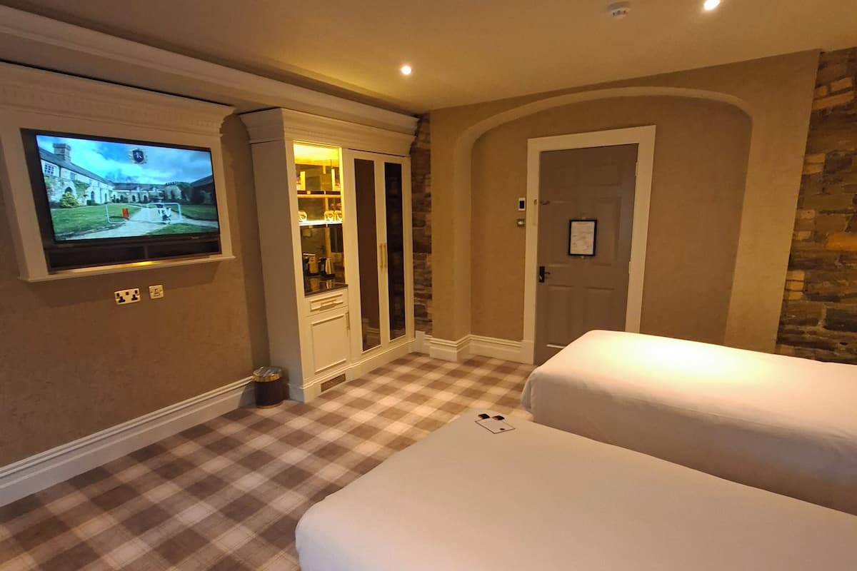 Quarto de hotel com televisão na parede, piso xadrez, cama e porta.