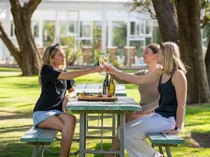 Três pessoas brindando com taças de vinho em uma mesa de piquenique em um parque.