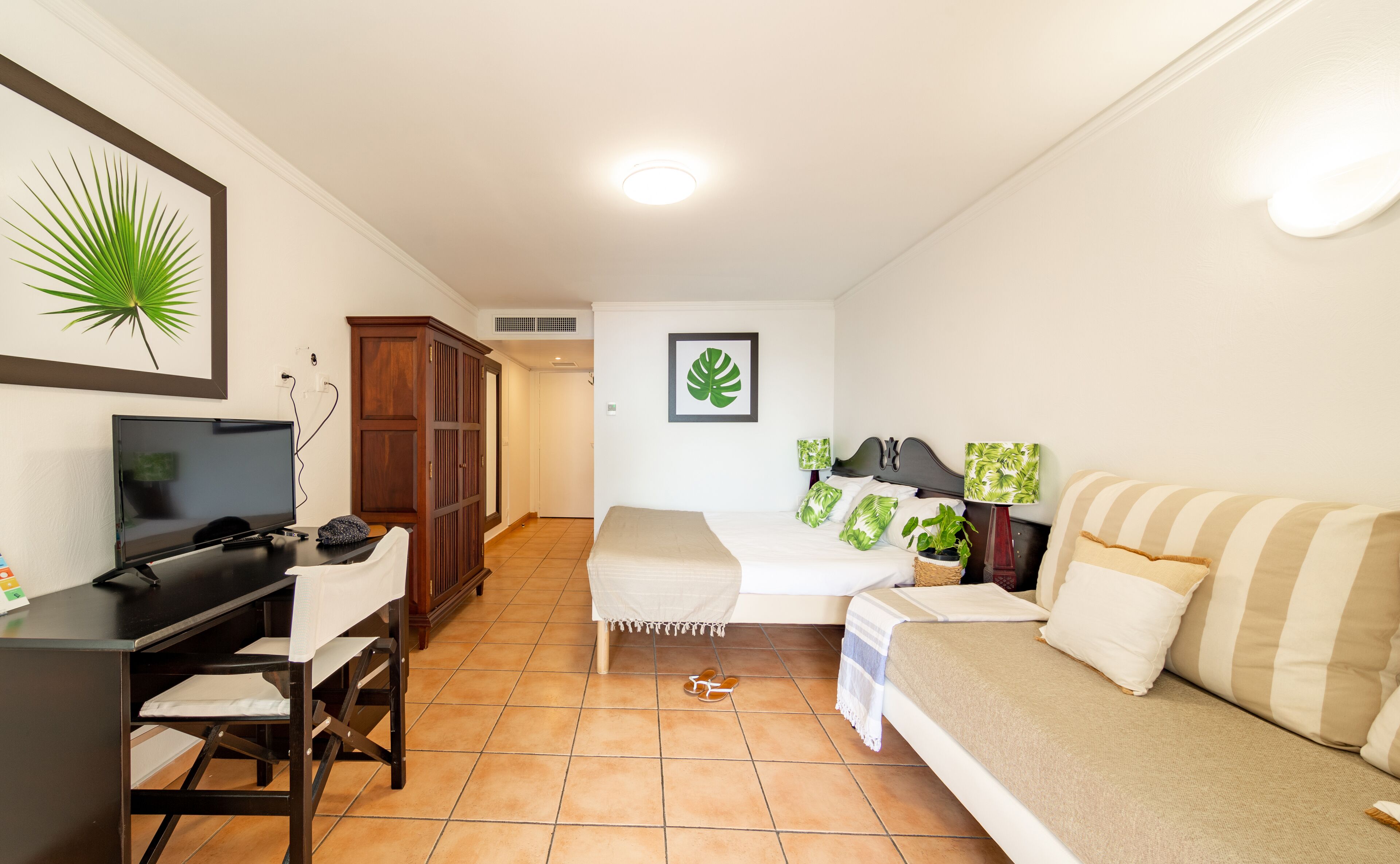 Quarto compacto com cama, escrivaninha e televisão.
