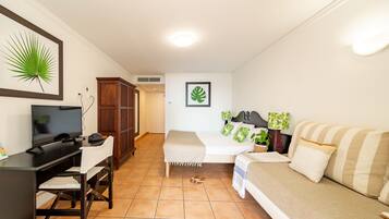 Quarto compacto com cama, escrivaninha e televisão.
