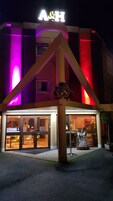 Um hotel com um letreiro A&H em destaque, uma grinalda de Natal e uma entrada visível com uma placa que diz 'CANAL+ LE BOUQUET'.