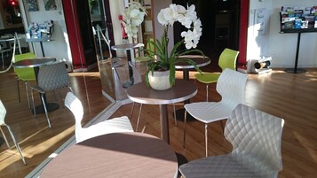 Decoração moderna com mesas redondas e cadeiras brancas acolchoadas, uma orquídea em vaso e uma estante com livros e revistas.