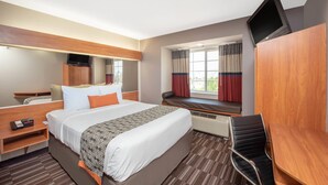Quarto de hotel com uma cama grande, uma mesa, uma cadeira, uma televisão e uma janela com cortinas.