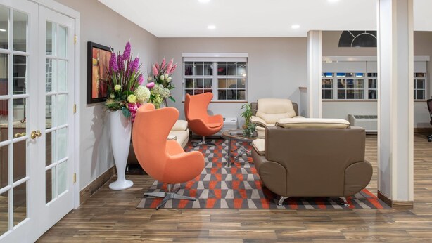 Um hall amplo com piso xadrez, um vaso branco grande com flores e cadeiras modernas cor de laranja.