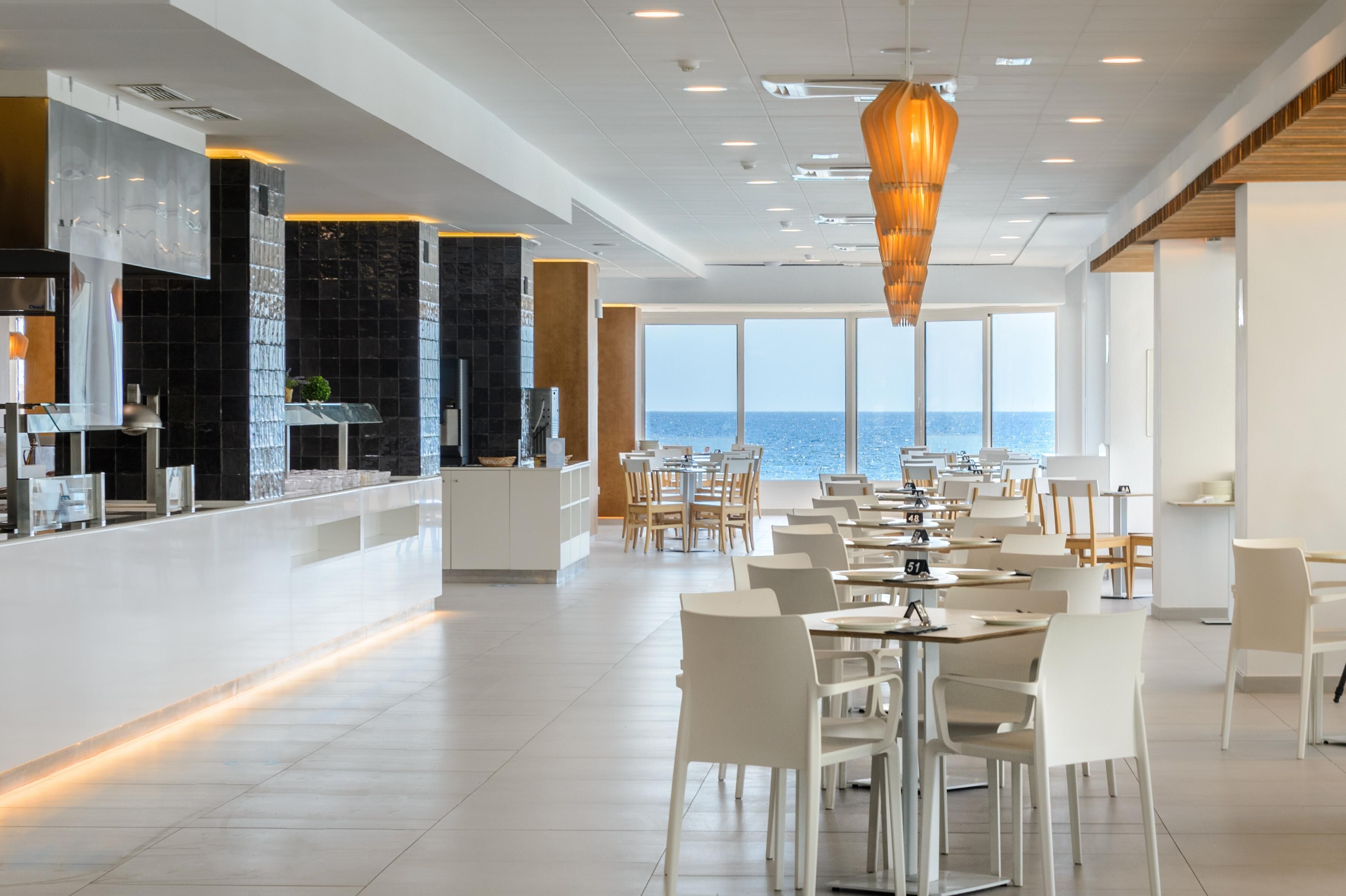 Uma ampla área de refeições com mesas e cadeiras, um balcão com vista para o mar e um design de interiores moderno.