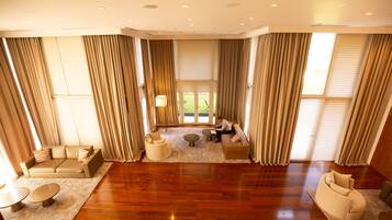 Uma sala de estar ampla, com piso de madeira, sofás bege e uma mesa de centro redonda.