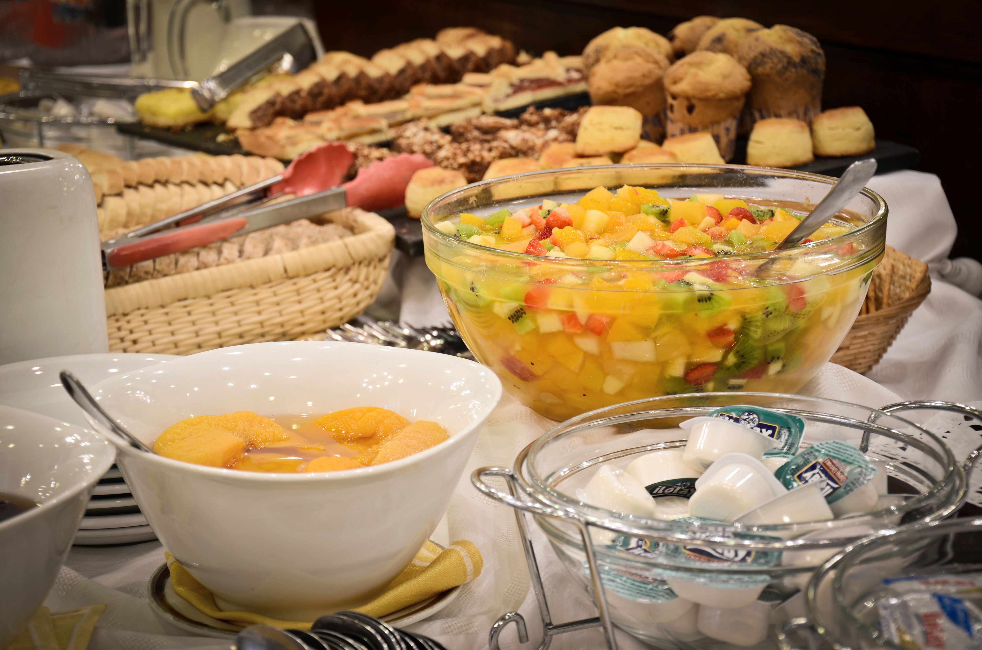 Buffet com diversos pratos, incluindo uma saladeira de salada de frutas, doces e uma tigela de sopa.