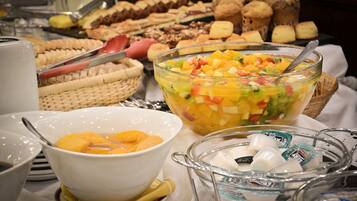 Buffet com diversos pratos, incluindo uma saladeira de salada de frutas, doces e uma tigela de sopa.