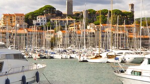 Um porto com vários barcos atracados, cercado por edifícios com telhados vermelhos e uma torre imponente ao fundo.