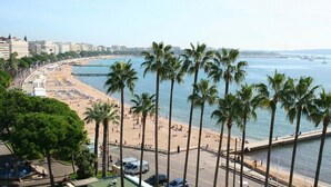 Uma praia com palmeiras, um calçadão e edifícios ao fundo.