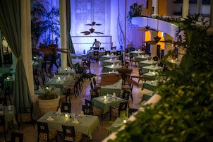 Restaurante com várias mesas preparadas para refeições, com ventoinha no teto e iluminação ambiente.