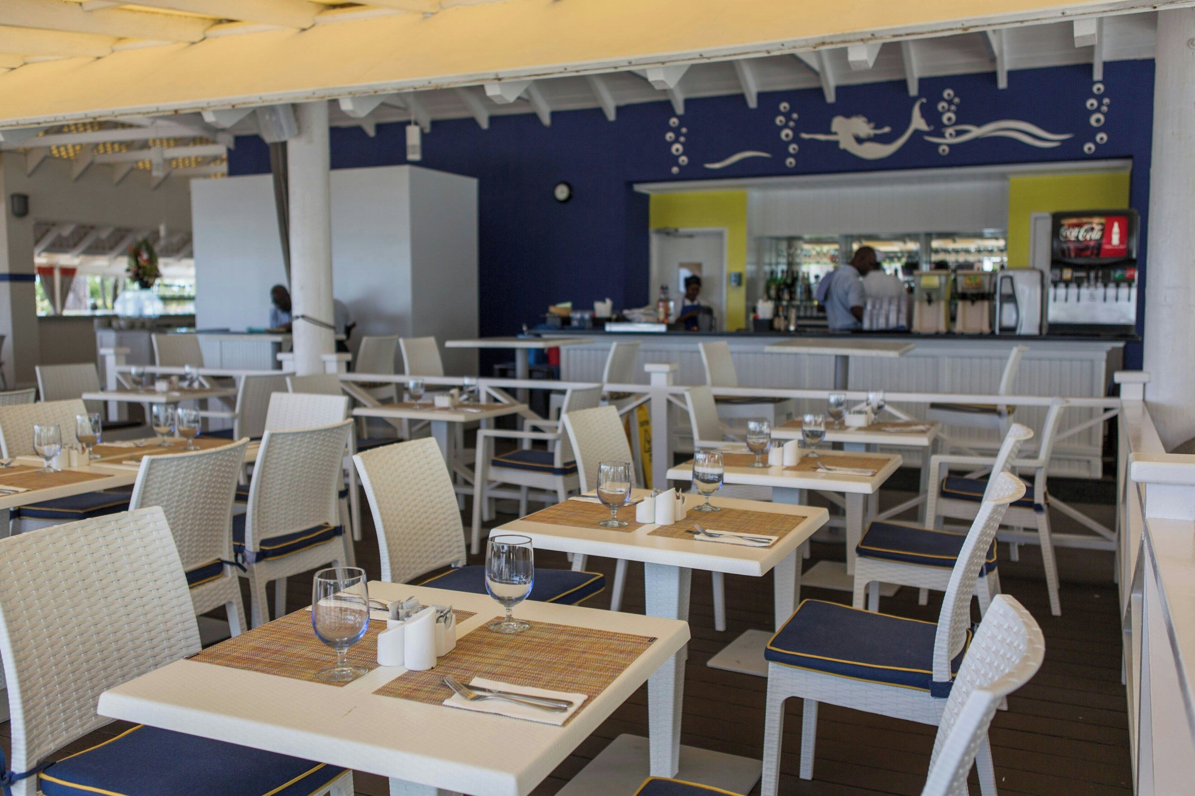 Um restaurante com mesas e cadeiras brancas, um bar ao fundo, e uma paleta de cores azul e branca.