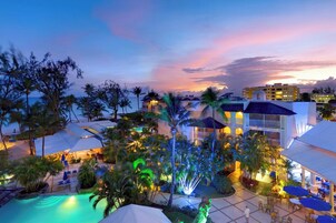 Um resort com piscina, palmeiras e um edifício com vários andares.