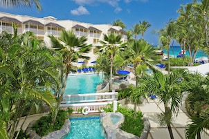 Um hotel com piscina, palmeiras e vista para o oceano.