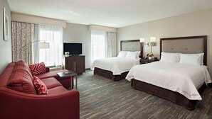 Quarto de hotel com sofá vermelho, duas camas, televisão e escrivaninha.