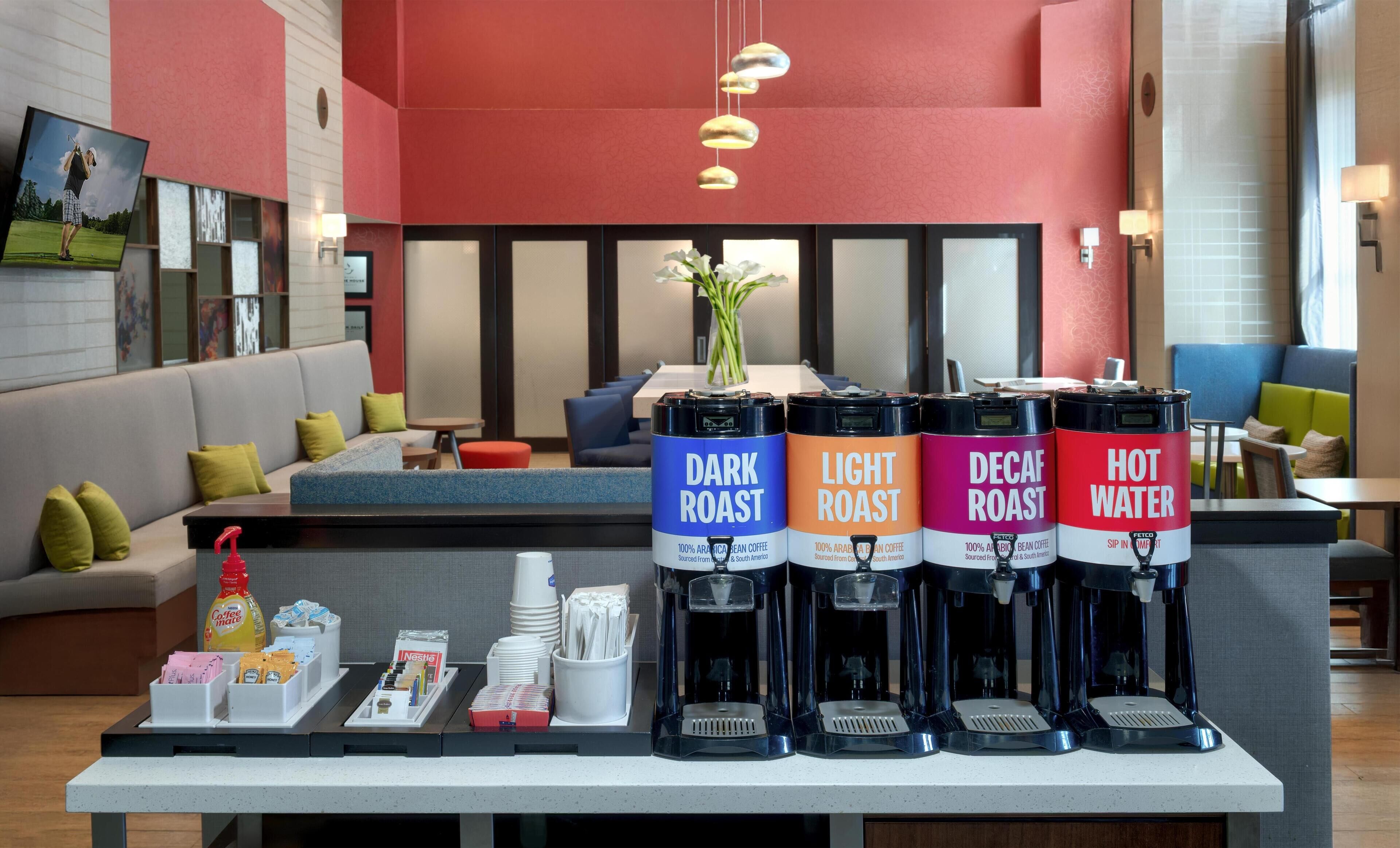 Uma estação de café com quatro máquinas de café identificadas como Torra Escura, Torra Clara, Descafeinado e Água Quente.