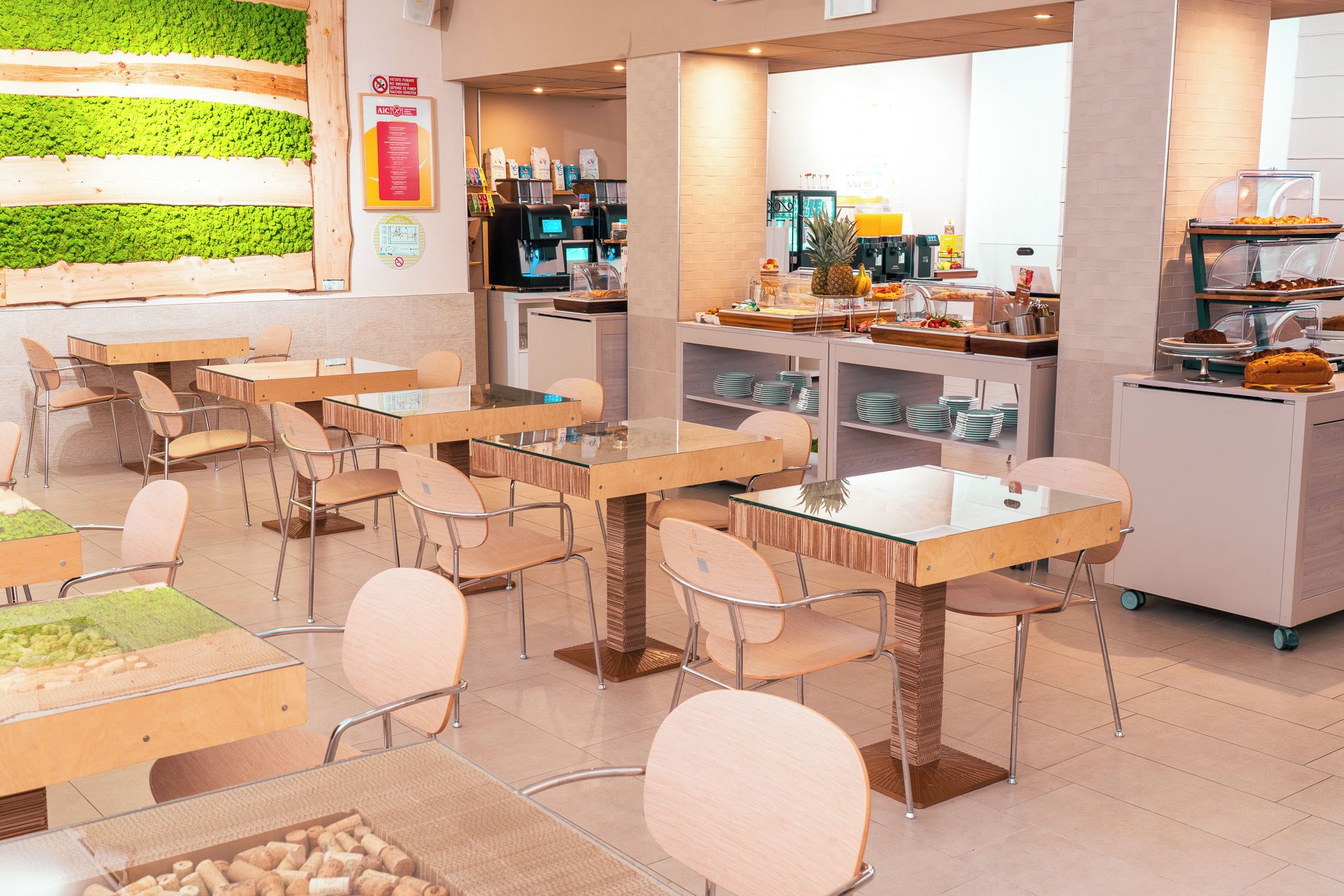 Um café moderno com várias mesas e cadeiras, uma máquina de café e um espaço para buffet com diversas opções de comida.