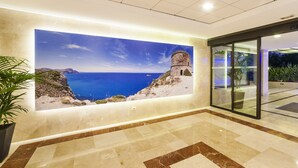 Um hall com um grande mural panorâmico, entrada por porta de vidro e piso de azulejos.
