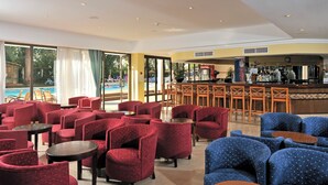 Um hall de hotel com cadeiras estofadas em vermelho e azul, vista para a piscina e área de bar.