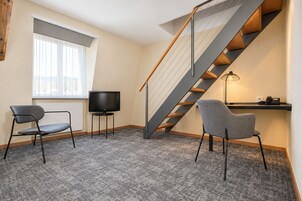 Quarto com escada moderna, televisão em suporte, duas cadeiras e escrivaninha com abajur.