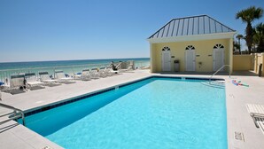 Piscina com água azul translúcida, um edifício com janelas em arco e vista para o oceano.