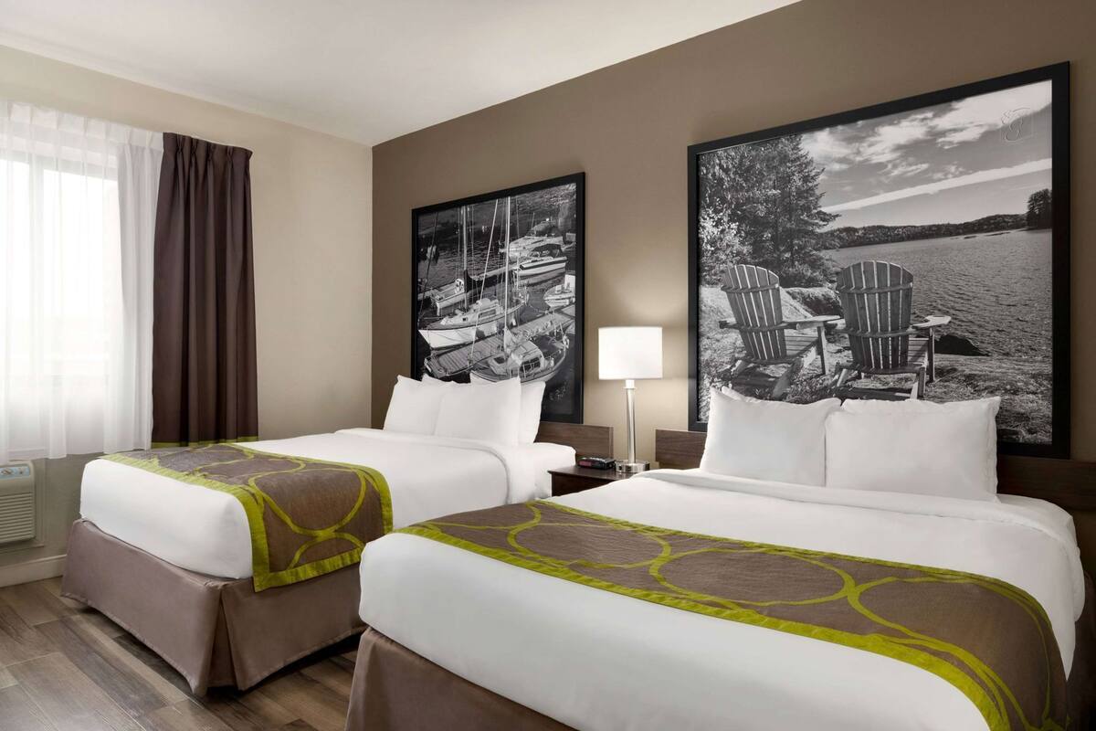 Quarto de hotel com duas camas, uma mesa de cabeceira, um abajur e duas fotografias grandes em preto e branco na parede.