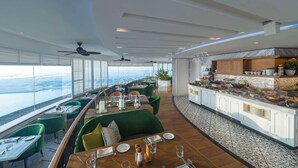 Restaurante moderno com vista alta da cidade, assentos verdes e uma área de buffet.