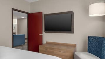 Quarto de hotel com cama, escrivaninha, cadeira, guarda-roupa, espelho e televisão.