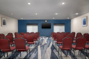 Uma sala de conferências com fileiras de cadeiras vermelhas, um carpete estampado e um relógio na parede.