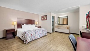 Quarto de hotel com cama, mesas de cabeceira, escrivaninha, cadeira, espelho e porta do banheiro.