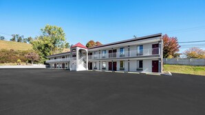 Um motel de dois andares com uma escadaria central, entrada coberta e estacionamento.