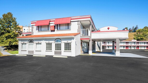 Um Red Roof Inn com um edifício de dois andares, uma área de estacionamento coberta e um céu azul límpido.