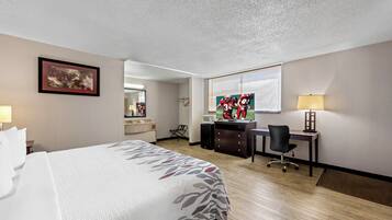 Quarto de hotel com uma cama grande, escrivaninha, cadeira, televisão e janela com persianas.
