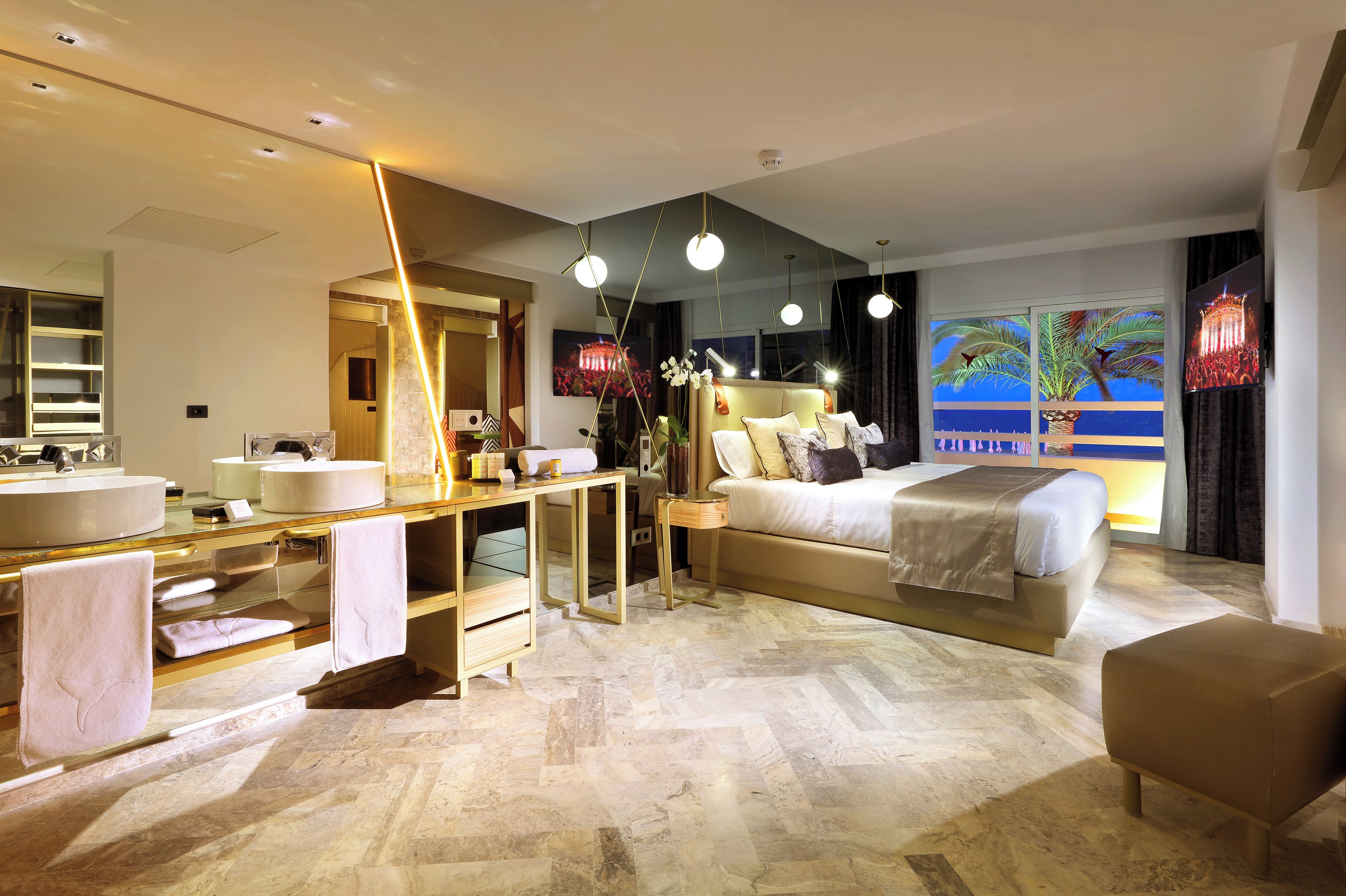 Quarto moderno com uma cama grande, mesas de cabeceira, toucador com espelho e vista para o oceano pela janela.