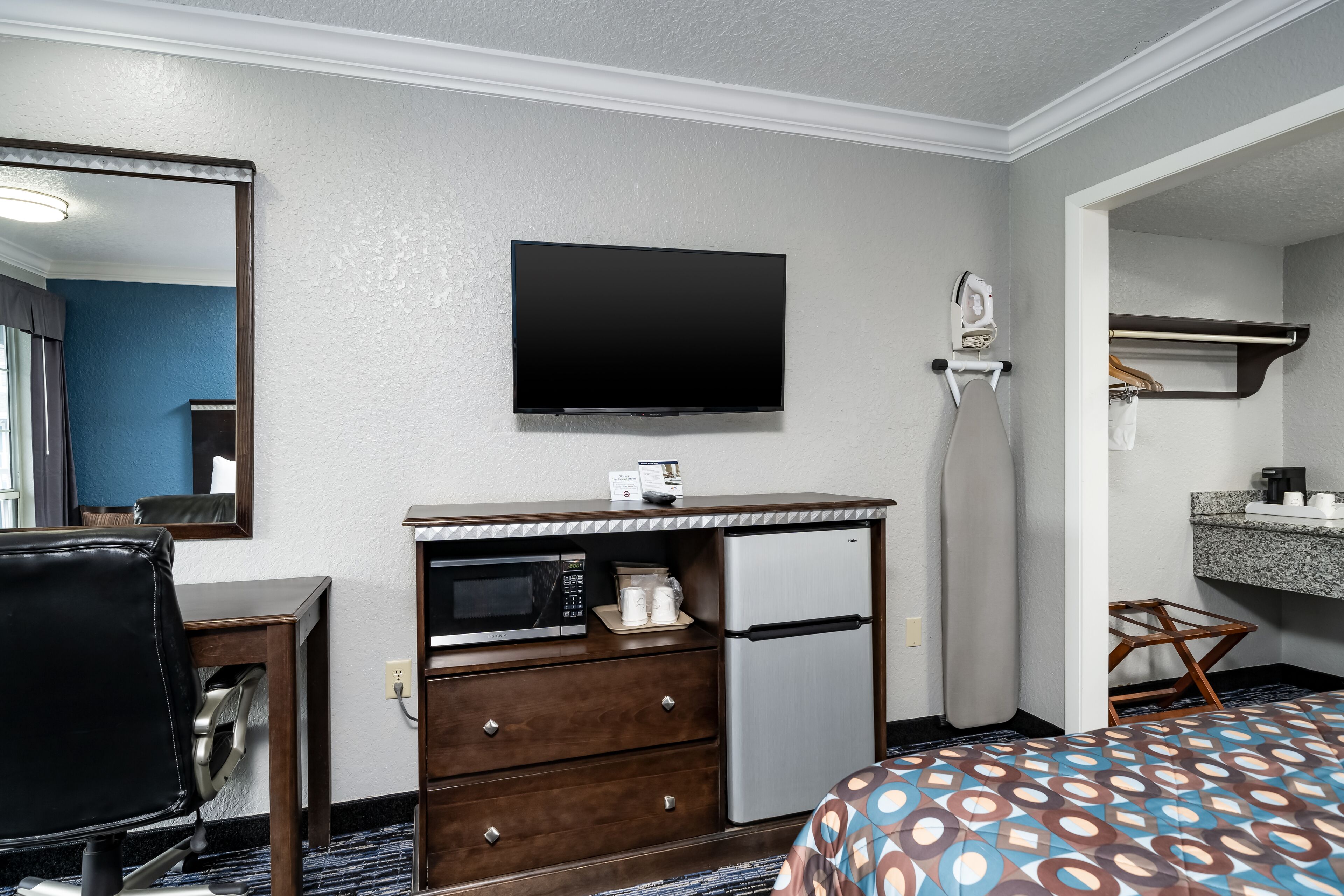 Quarto de hotel com uma cama, uma escrivaninha equipada com micro-ondas, frigorífico, televisão, espelho e casa de banho com chuveiro.